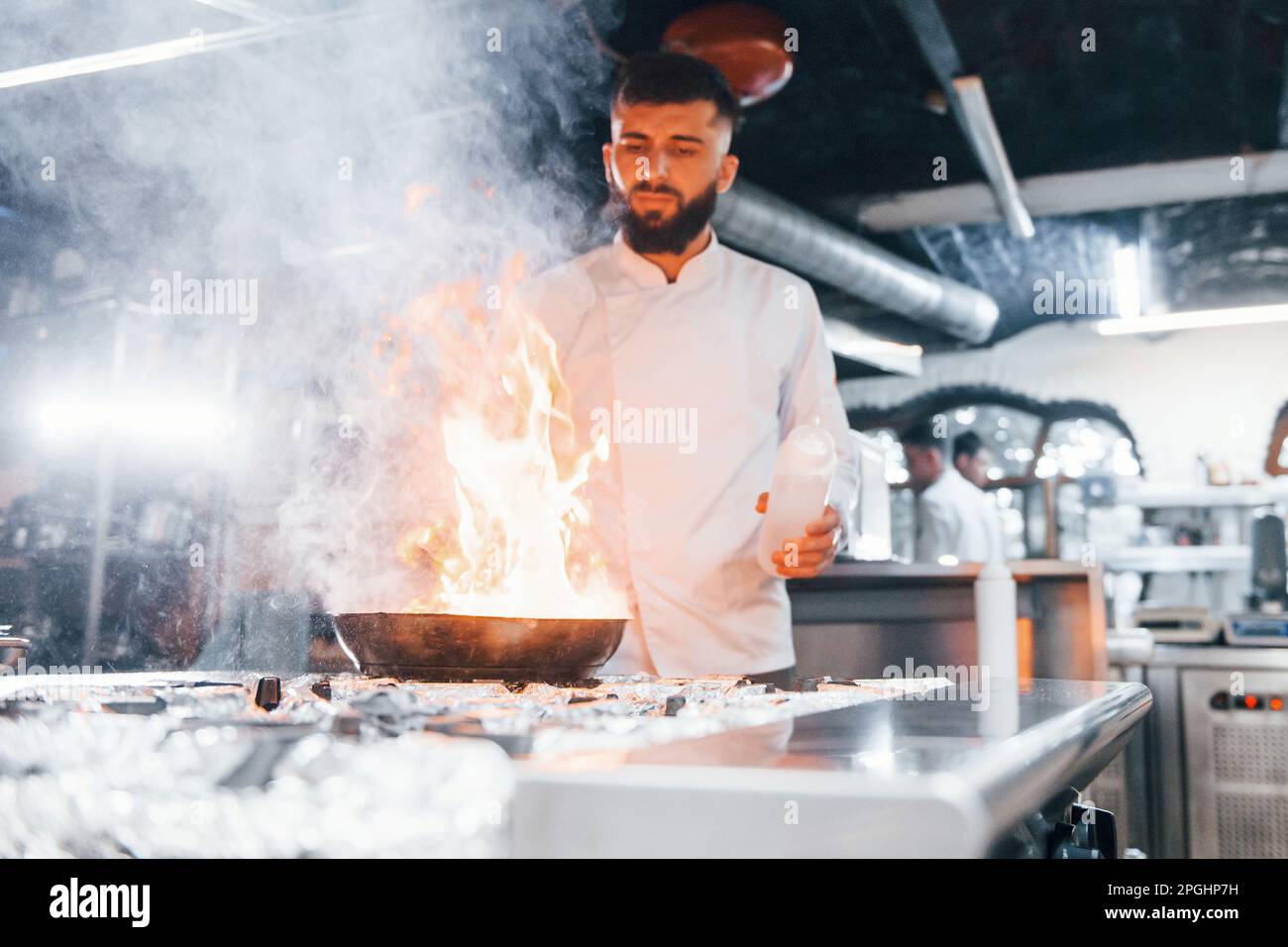 Uses frying pan. Chef in white uniform cooking food at kitchen. Busy ...