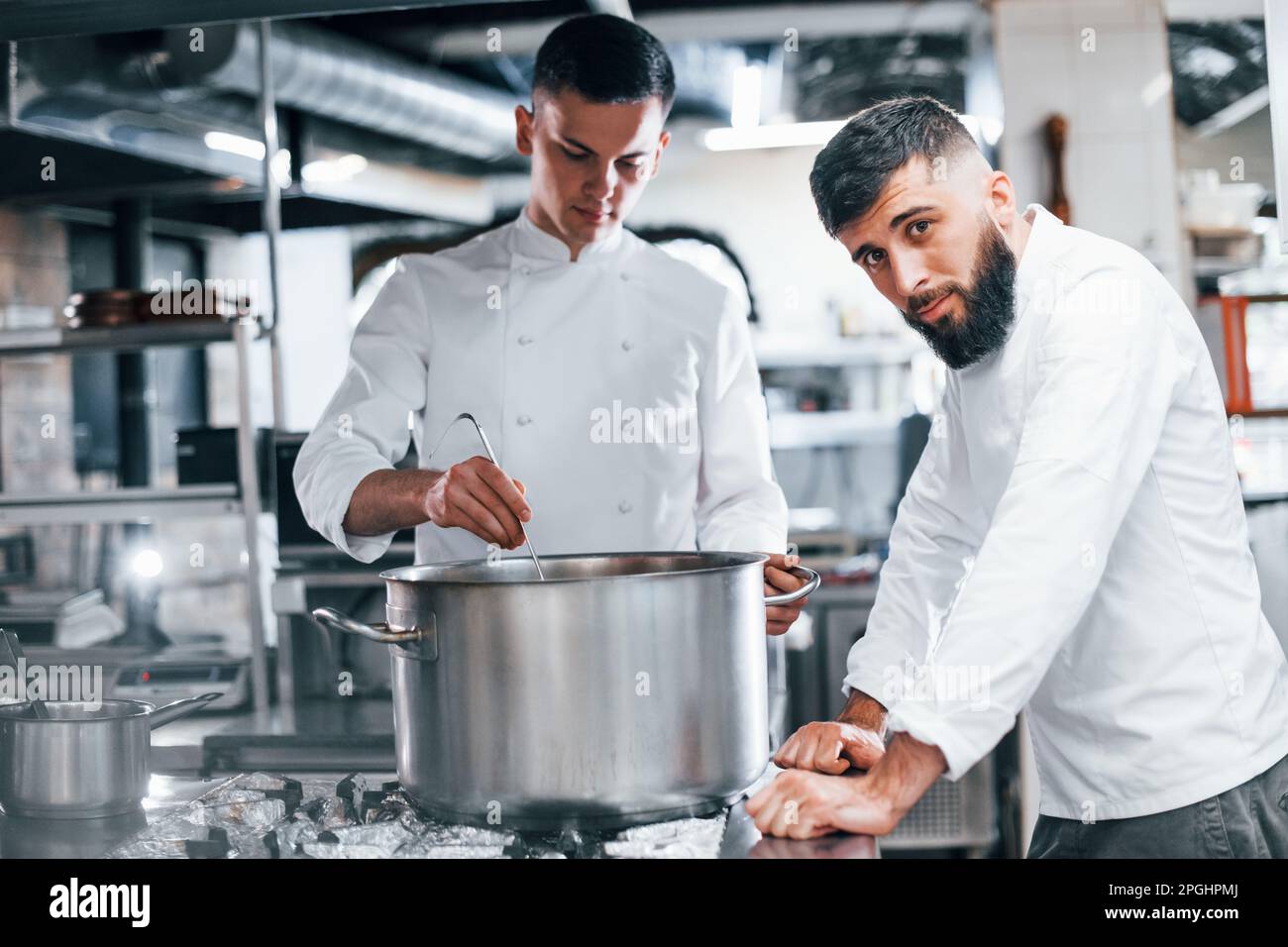 With help from other employee. Chef in white uniform cooking food at ...