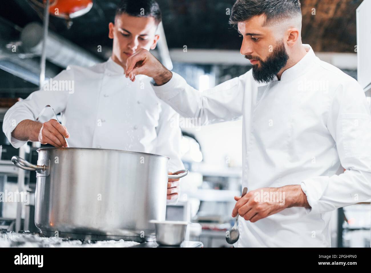 With help from other employee. Chef in white uniform cooking food at ...