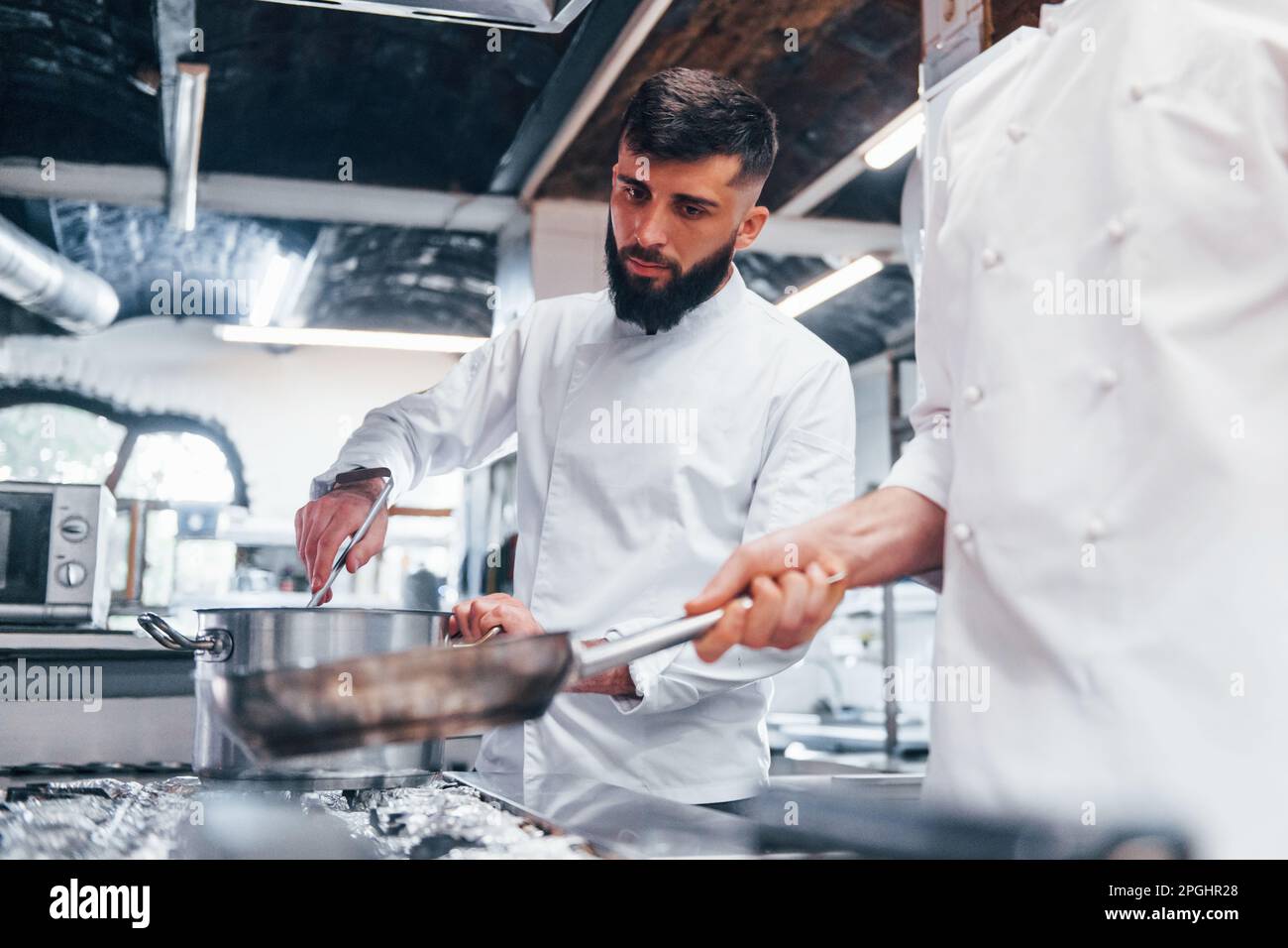 People in white uniform cooking food at kitchen together. Busy day at ...