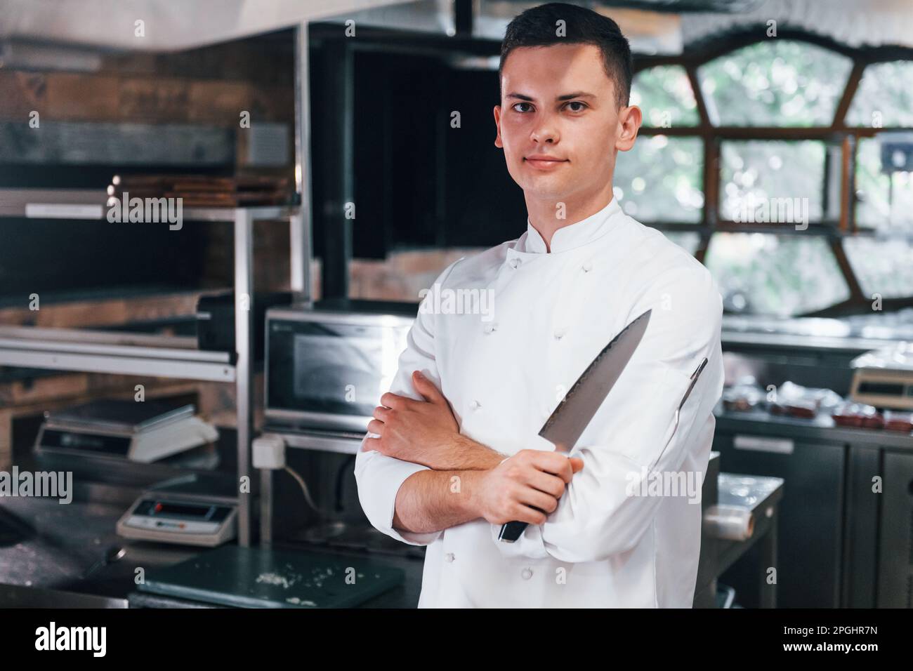 Chef in white uniform standing at kitchen. Holding knife in hands Stock ...