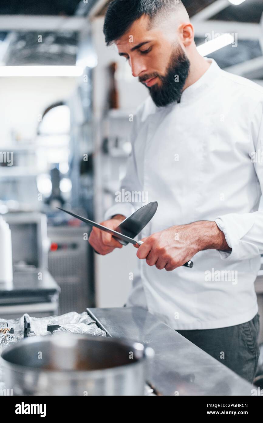 Chef in white uniform standing at kitchen. Holding knives in hands ...