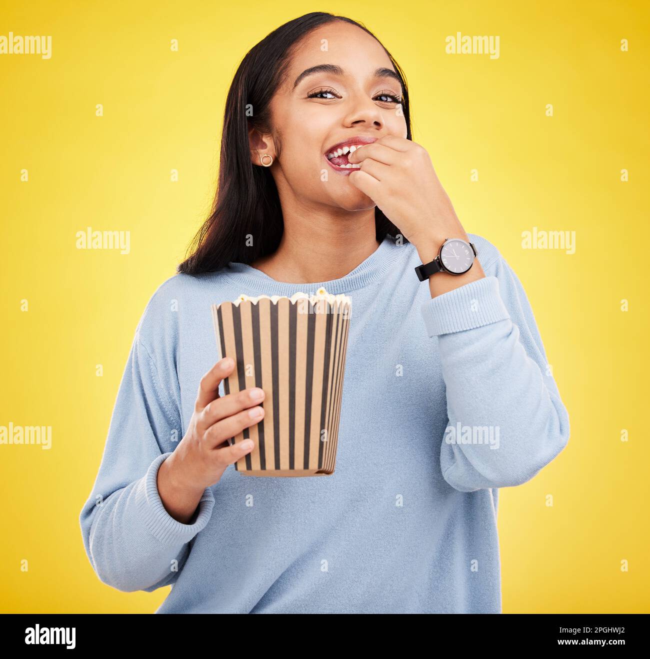 Happy woman is eating popcorn, watching tv and portrait, box with snack for movie on yellow ...