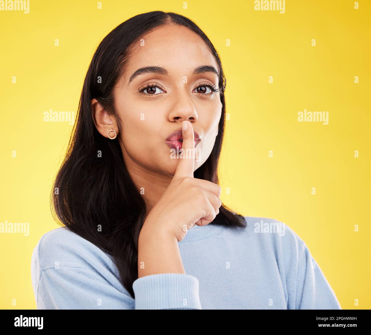 Secret, portrait and woman with finger on lips in studio, yellow ...