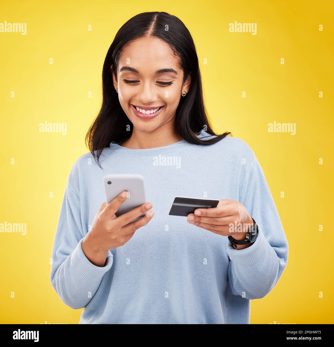 Woman with smartphone, credit card and ecommerce with smile and online shopping on yellow studio ...