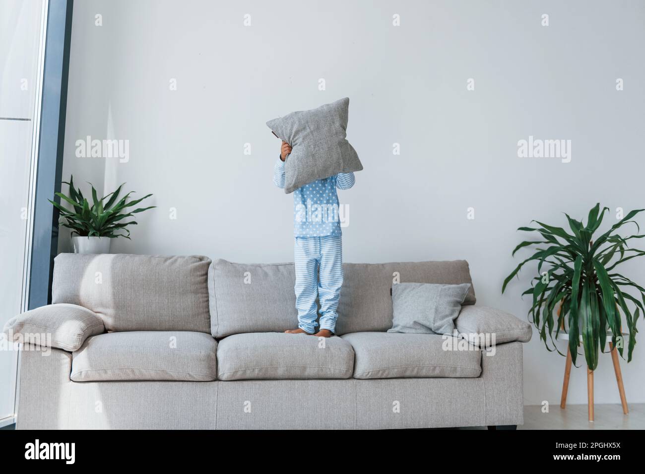 Jumping on the sofa. Cute little girl indoors at home alone. Child ...