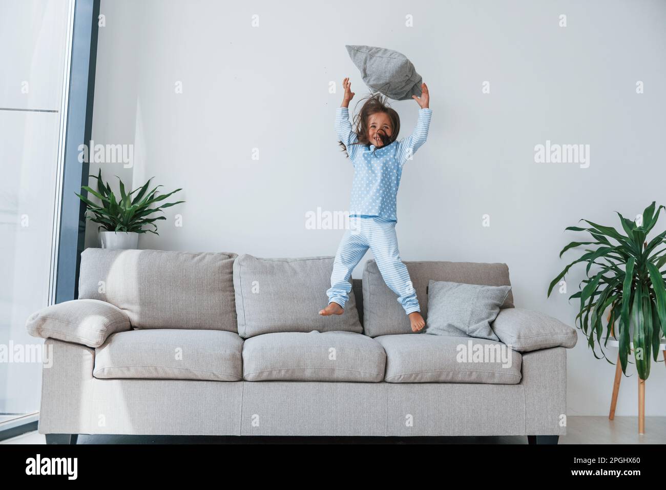 Jumping on the sofa. Cute little girl indoors at home alone. Child ...
