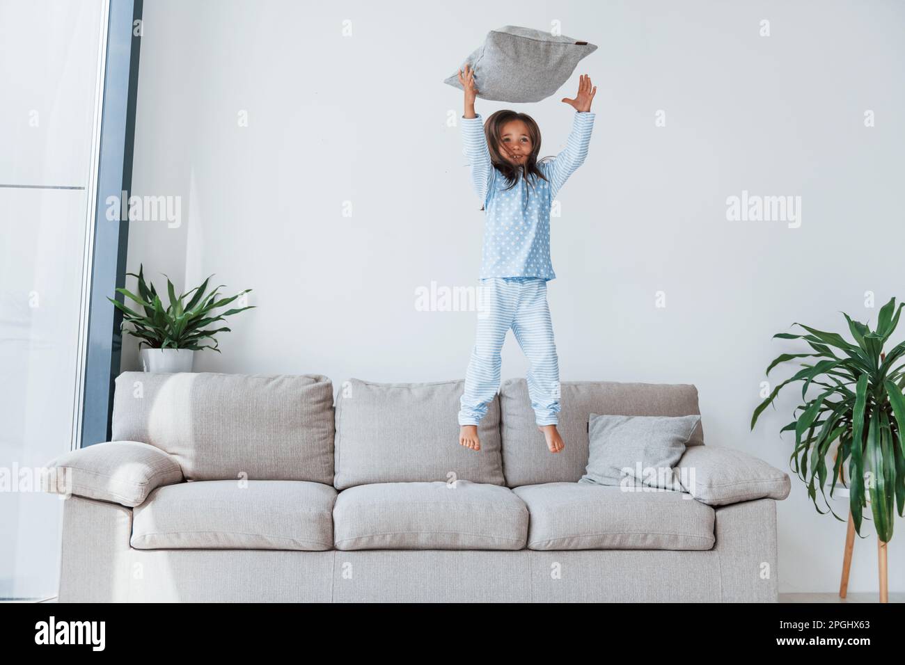 Jumping on the sofa. Cute little girl indoors at home alone. Child ...