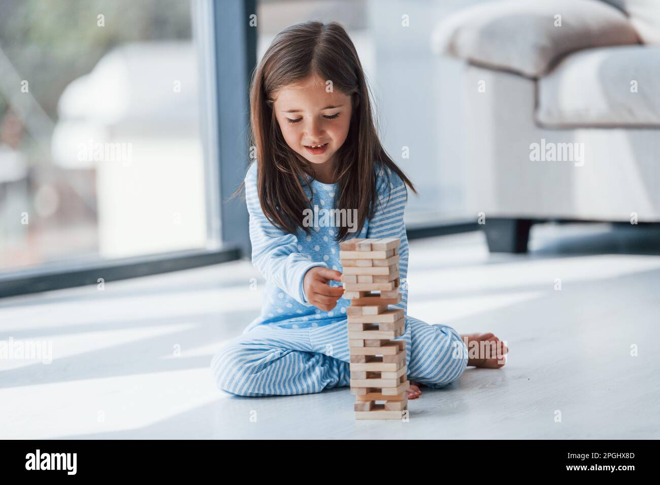 Plays tower game. Cute little girl indoors at home alone. Child ...