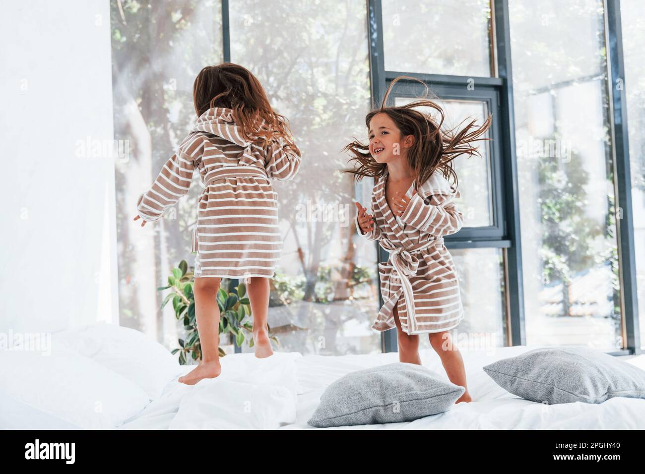 Jumping on bed. Two cute little girls indoors at home together ...