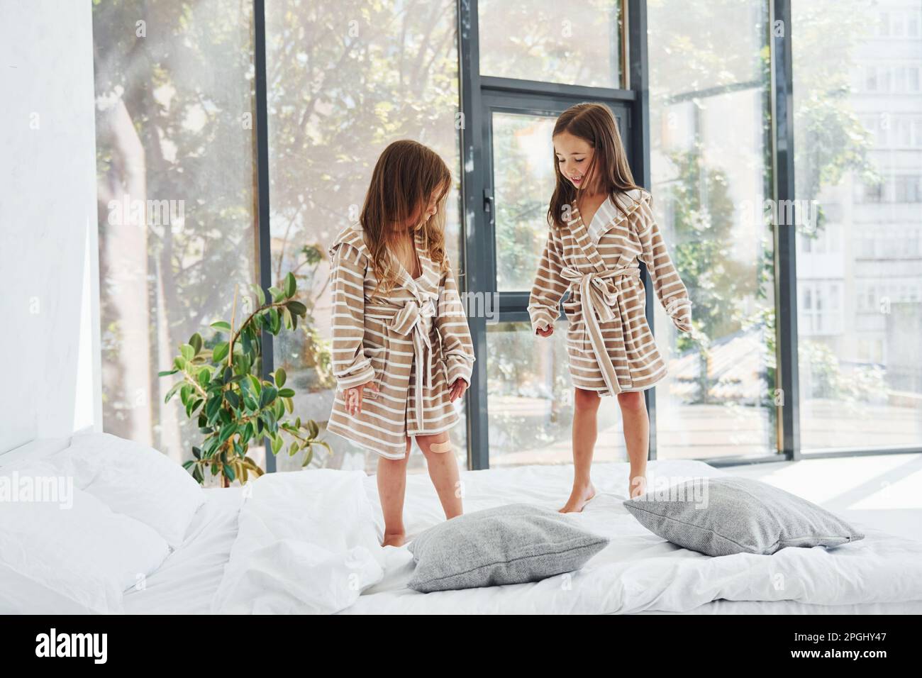 Jumping on bed. Two cute little girls indoors at home together ...