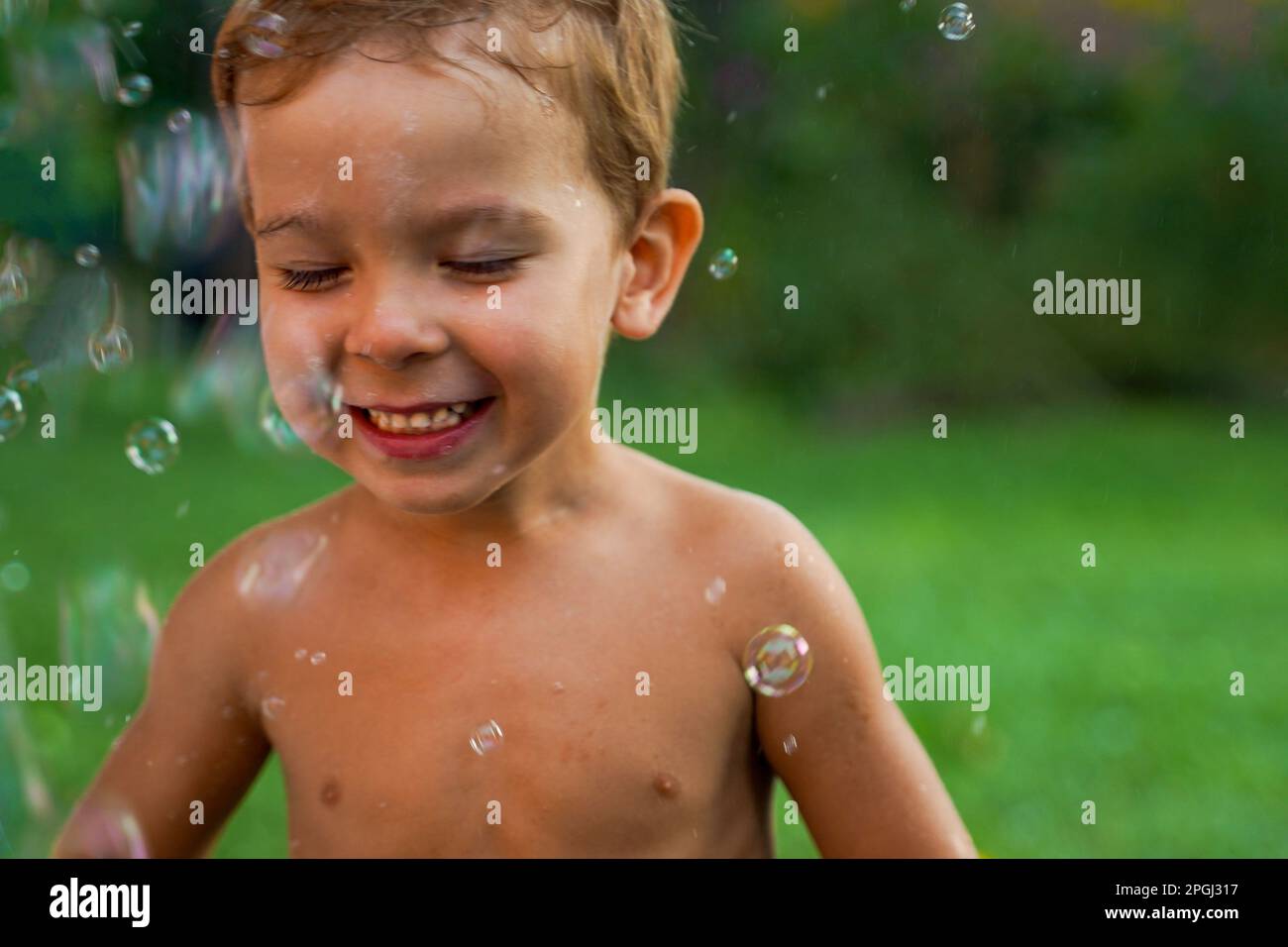 A little boy without clothes happily stands in a stream of flying soap ...