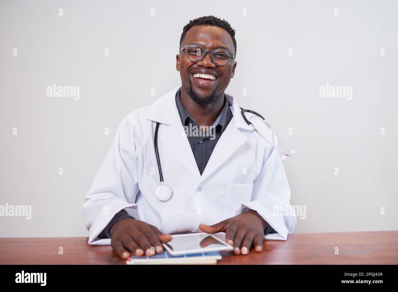 Candid portrait of a Black doctor in lab coat sitting at desk plain ...