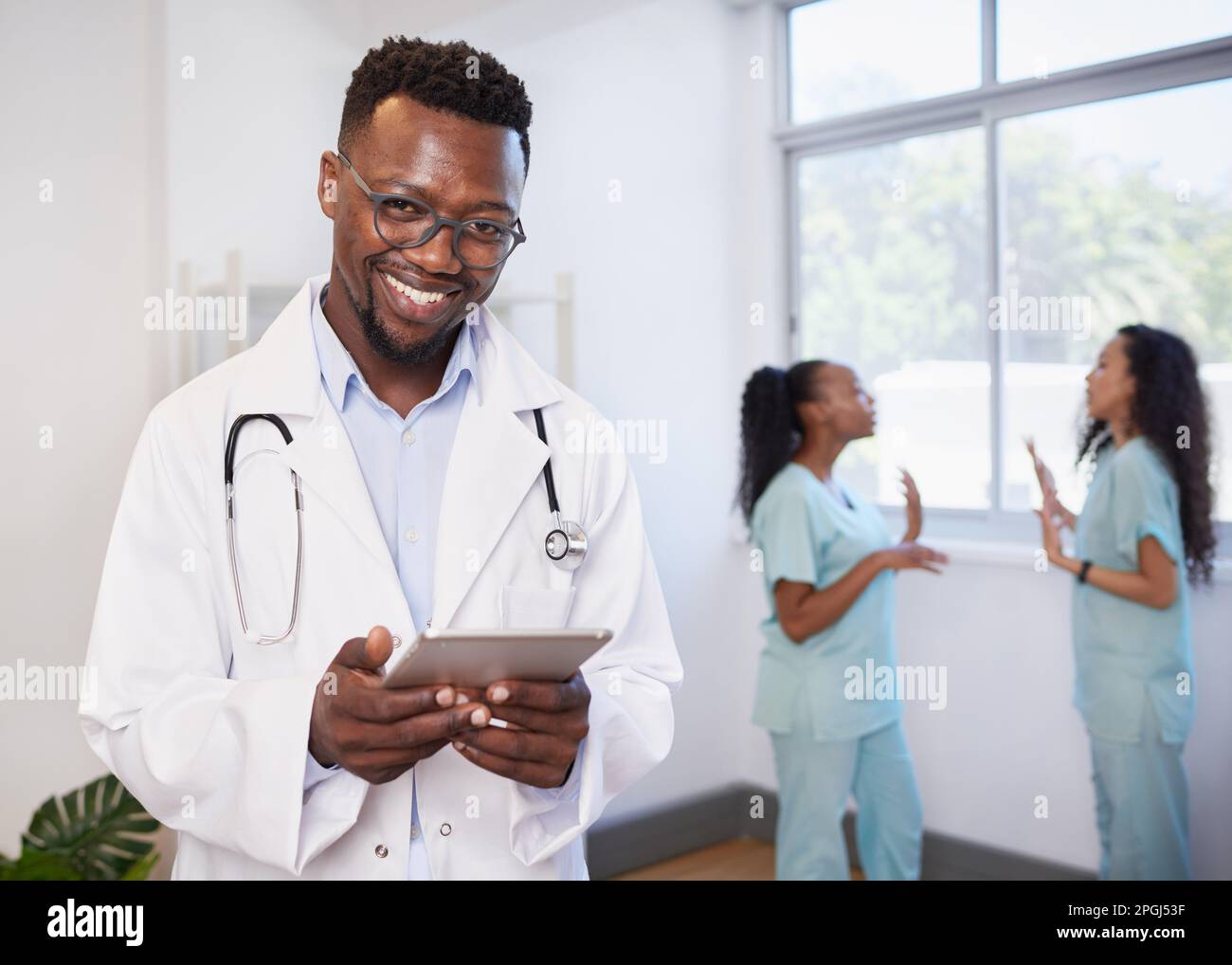 Portrait of Black doctor holding digital tablet, with nurses in ...