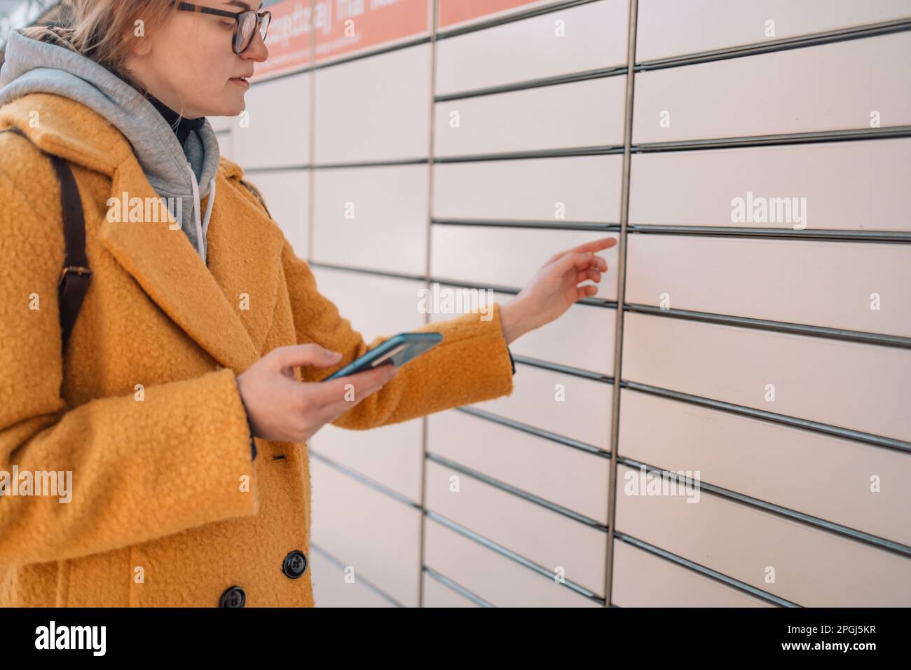 Pickup parcel. Young caucasian woman holding smartphone near automatic ...