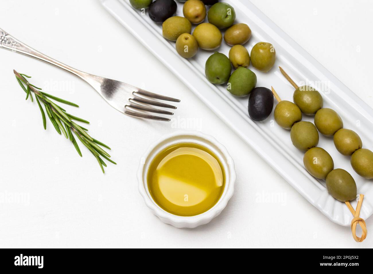 Green olives in a white plate. Olive oil in a small bowl. Fork and ...
