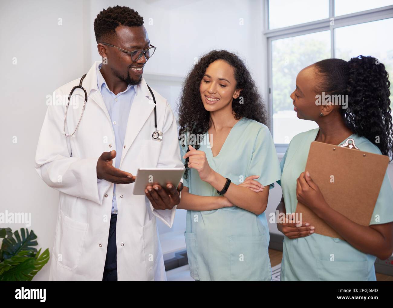 Three healthcare professionals stand in a row discussing patient case ...