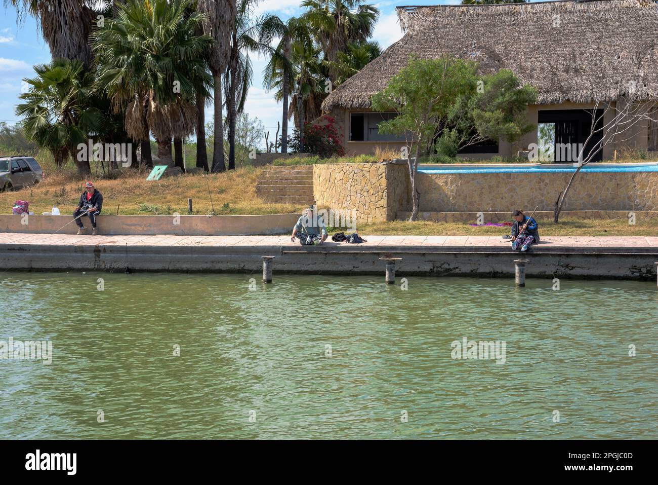 Three people sit along the Rio Grande River on the Mexican side of the ...