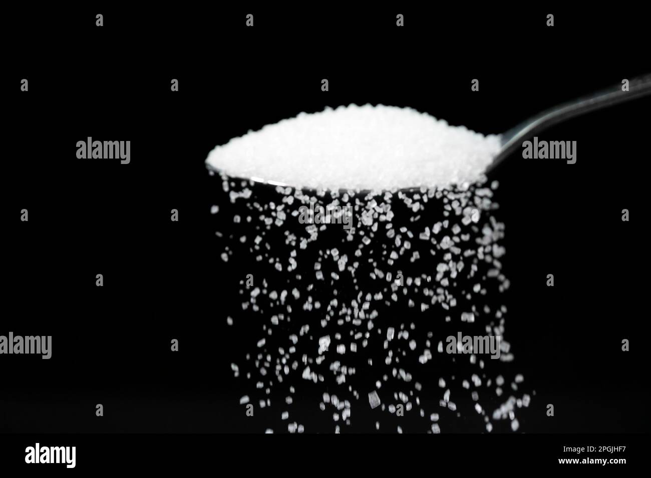 Macro photography of a teaspoon with white sugar on a black background ...