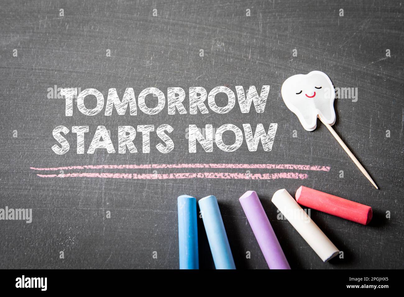 Tomorrow starts Now. Text and colored pieces of chalk on a dark board ...