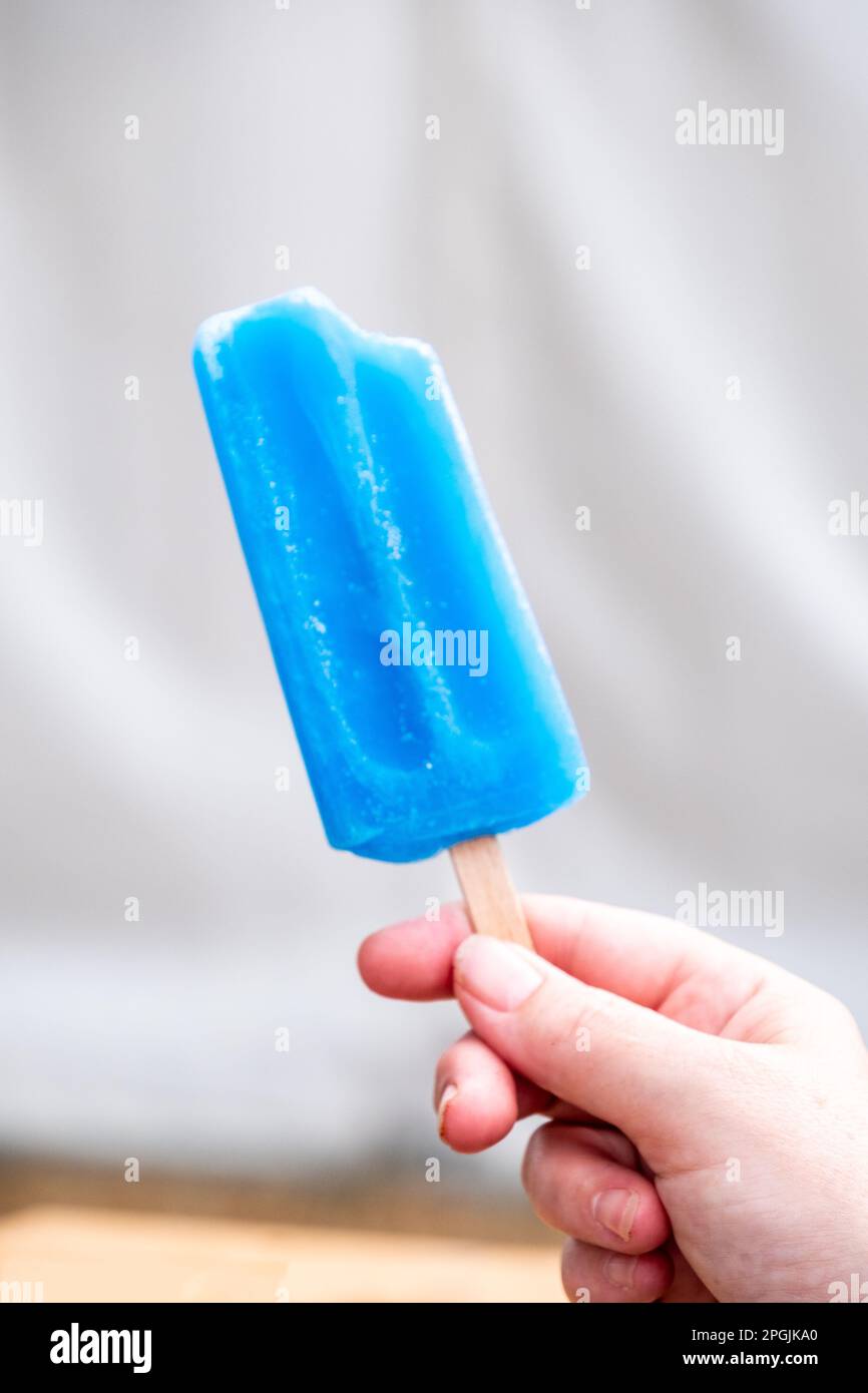 A womans hand holding a partly nibbled blue ice lolly at a village fete ...