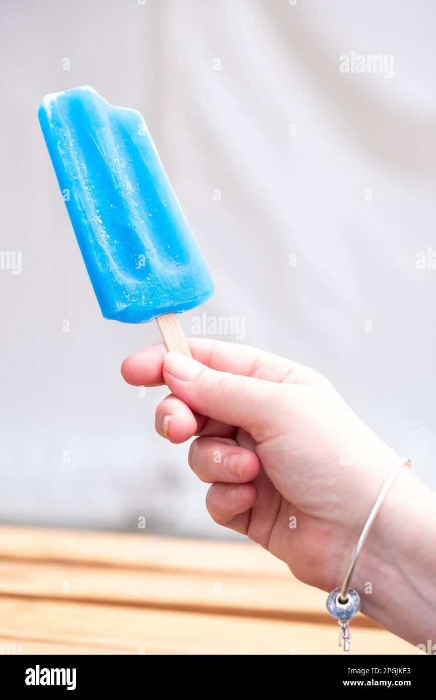 A womans hand holding a partly nibbled blue ice lolly at a village fete ...