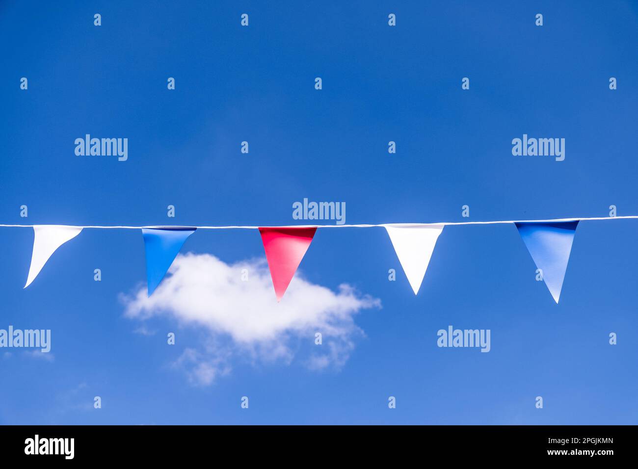 A string of red, white and blue bunting flags against a summer sky at a ...