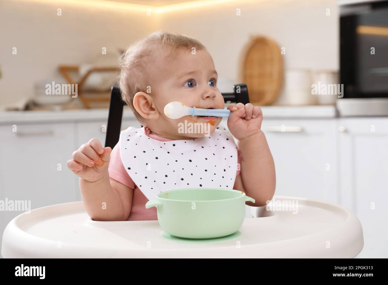 Cute little baby eating food in high chair at kitchen Stock Photo - Alamy