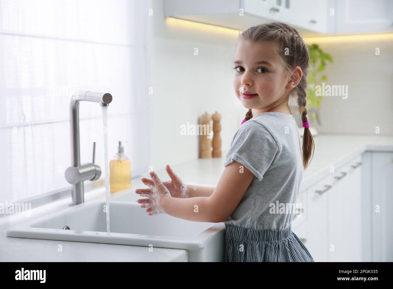Cute little girl washing hands with liquid soap in kitchen Stock Photo ...