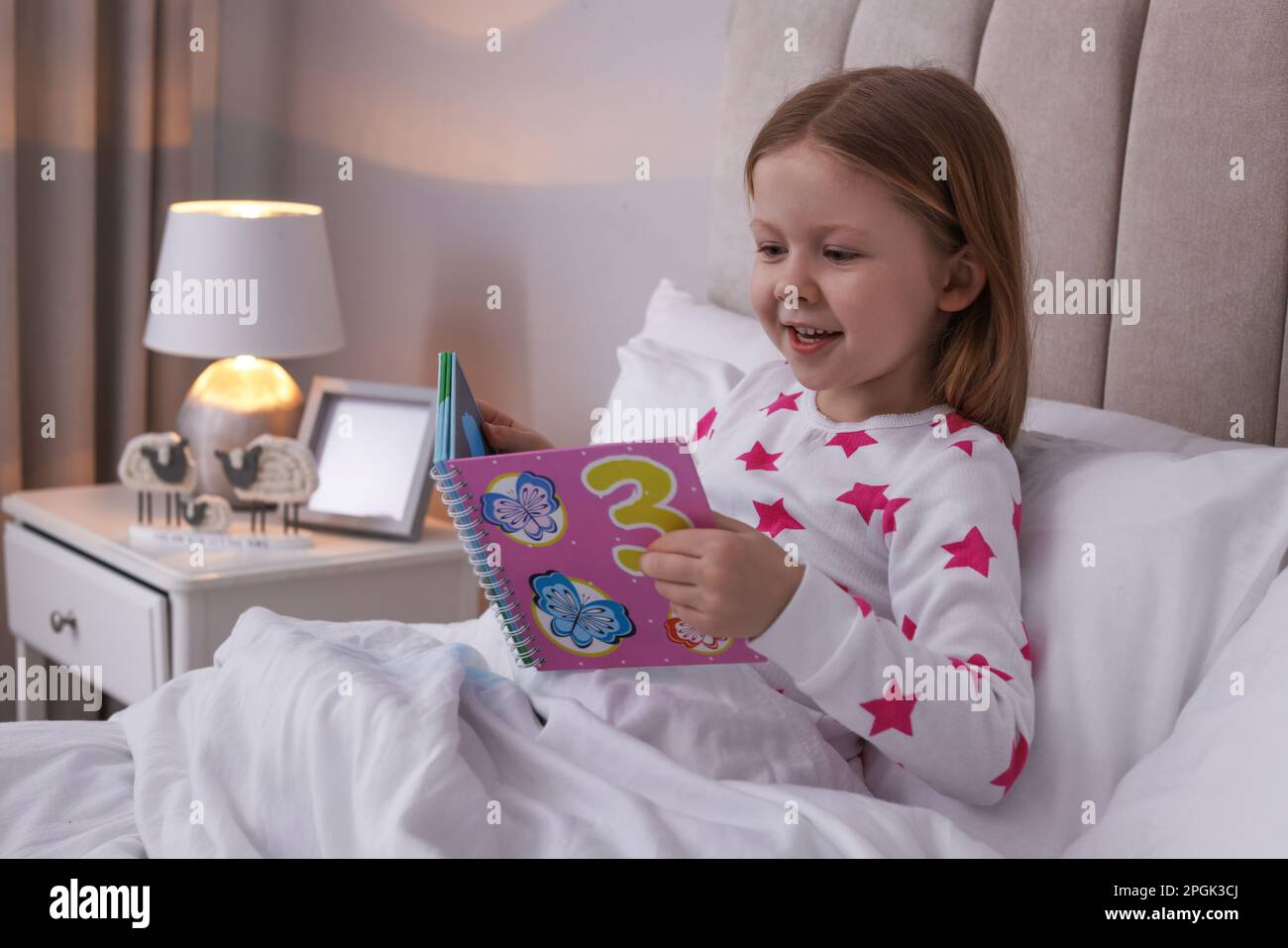 Cute little girl reading book in bed at home Stock Photo - Alamy