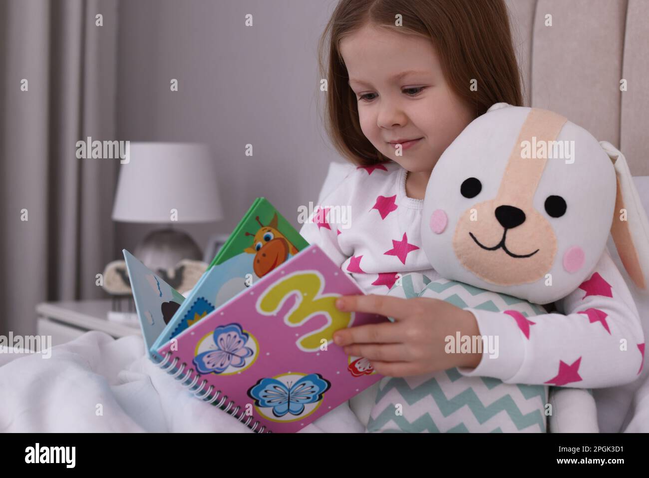 Cute little girl with toy reading book in bed at home Stock Photo - Alamy