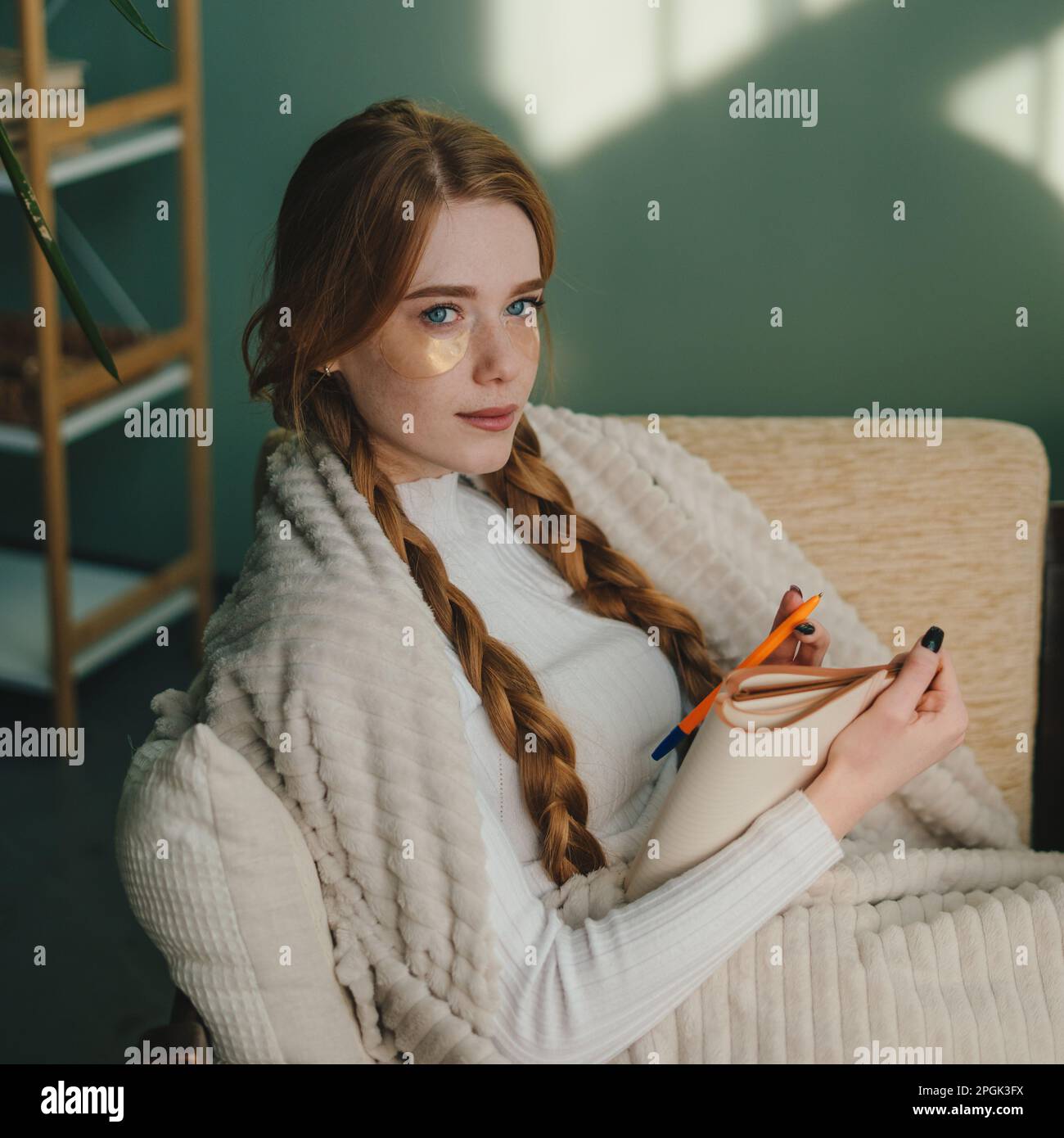 Ginger woman thinking and writing notes on a notebook, sitting on sofa ...