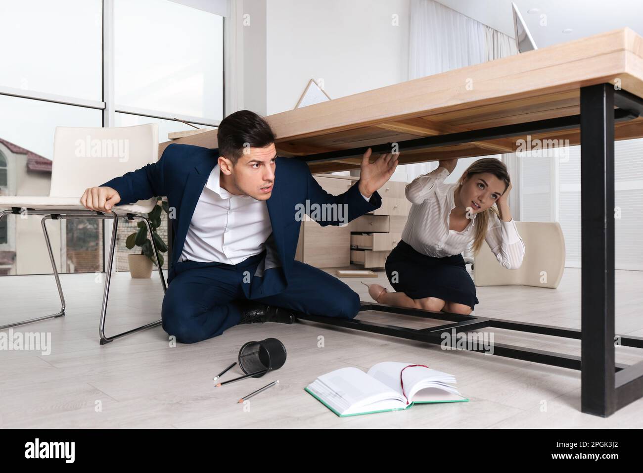 Scared employees hiding under office desk during earthquake Stock Photo ...