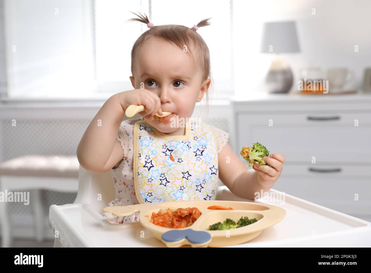 Cute little baby eating food in high chair at home Stock Photo - Alamy
