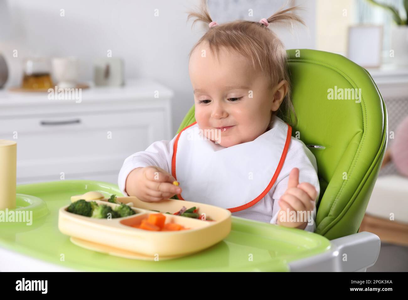 Cute little baby eating food in high chair at home Stock Photo - Alamy