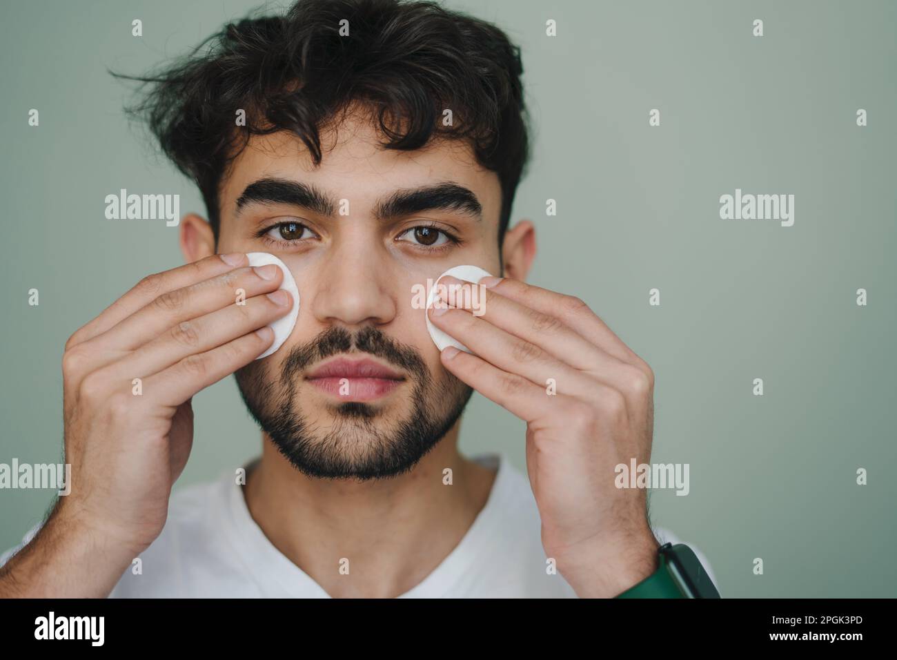 Front view portrait of a handsome man cleaning face skin with cotton ...