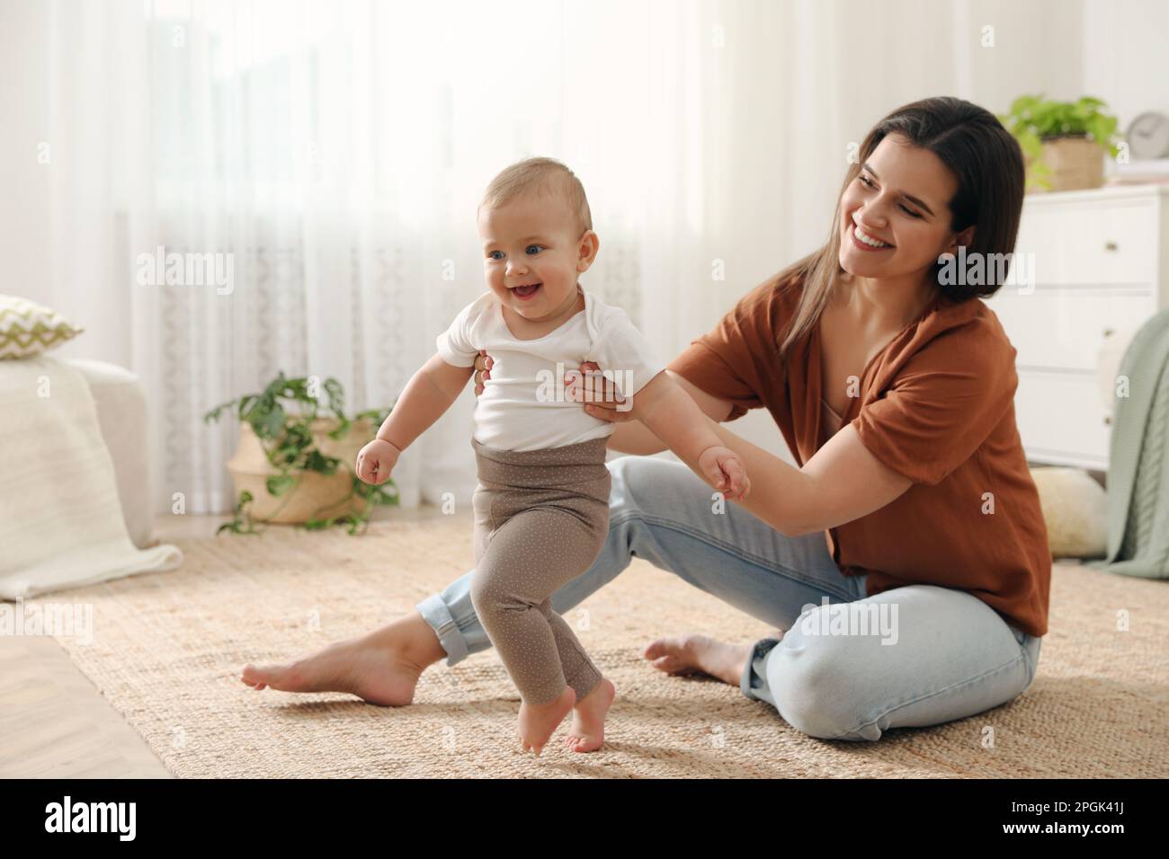 Mother supporting her baby daughter while she learning to walk at home ...