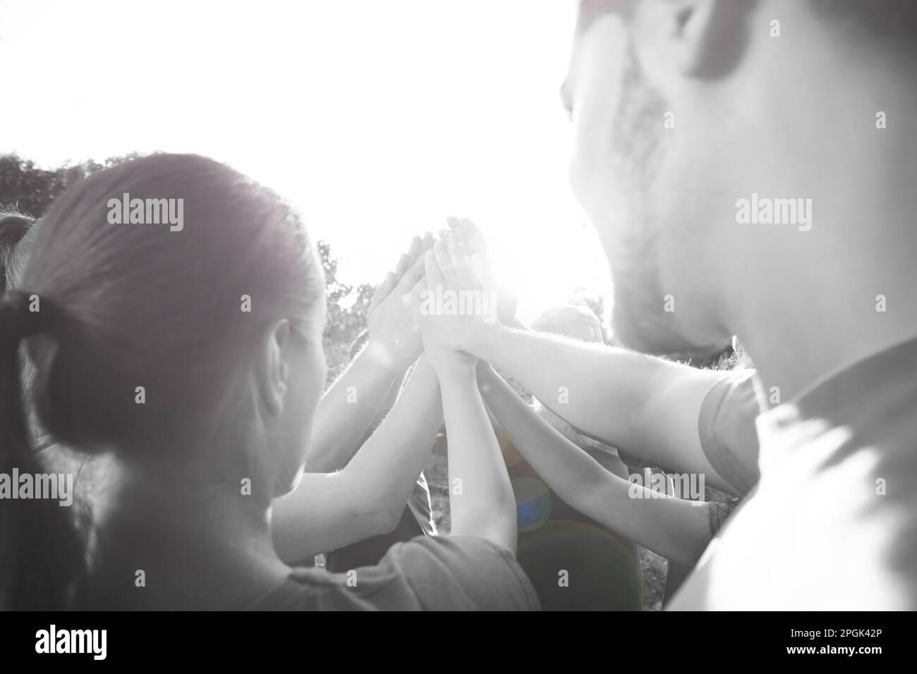 Group of volunteers joining hands together outdoors. Black and white ...