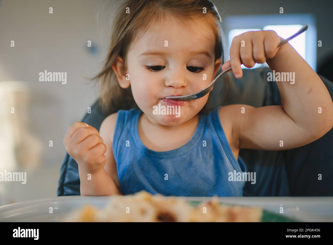 Caucasian baby girl eating lunch alone, sitting on high-chair. Happy ...