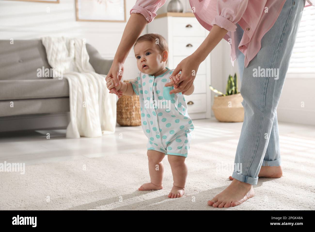 Mother supporting her baby daughter while she learning to walk at home ...