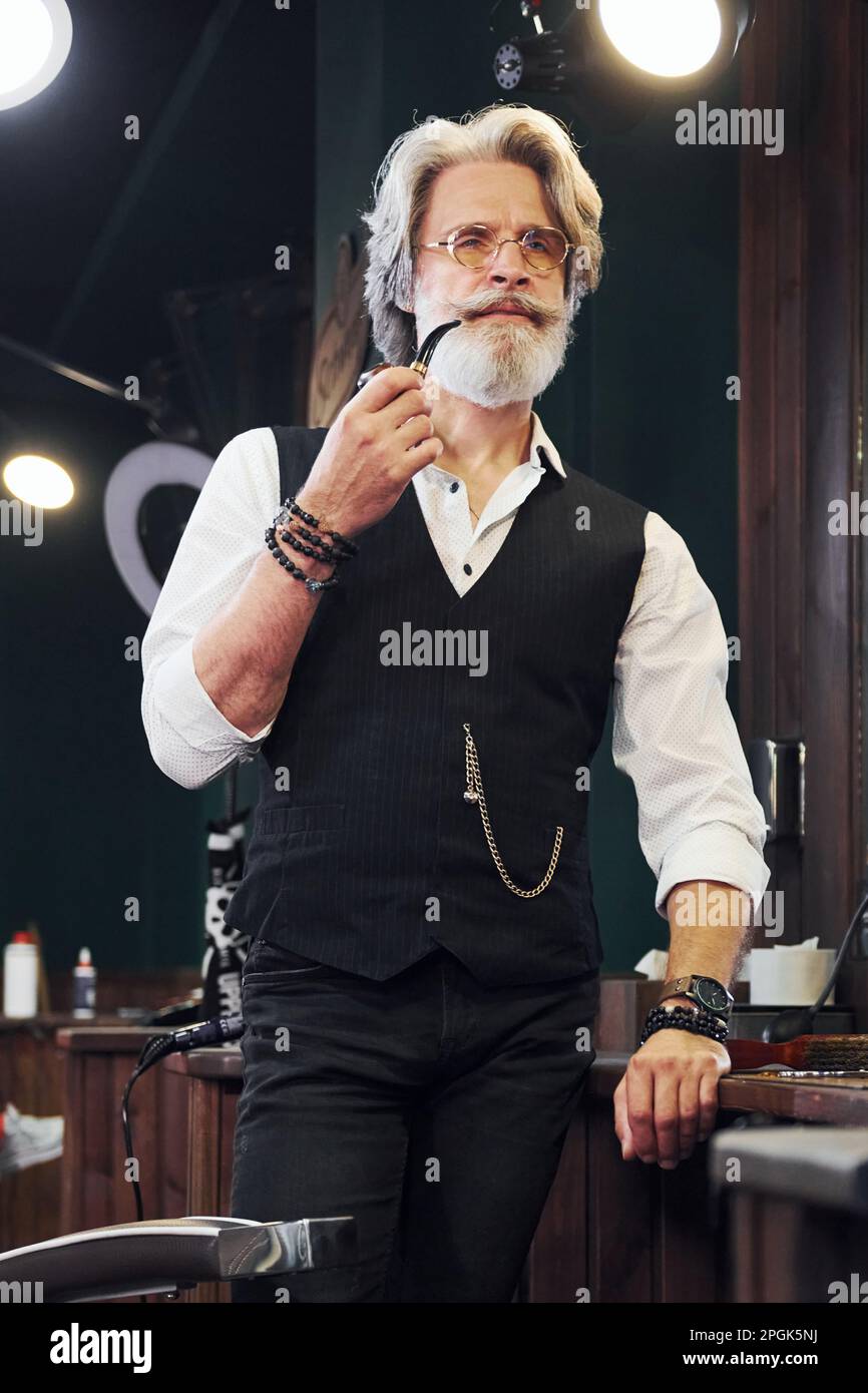 Standing and smoking in barbershop. Stylish modern senior man with gray ...