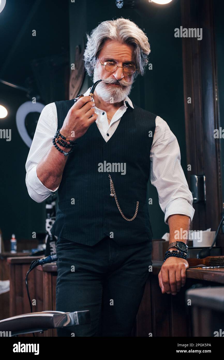 Standing and smoking in barbershop. Stylish modern senior man with gray ...