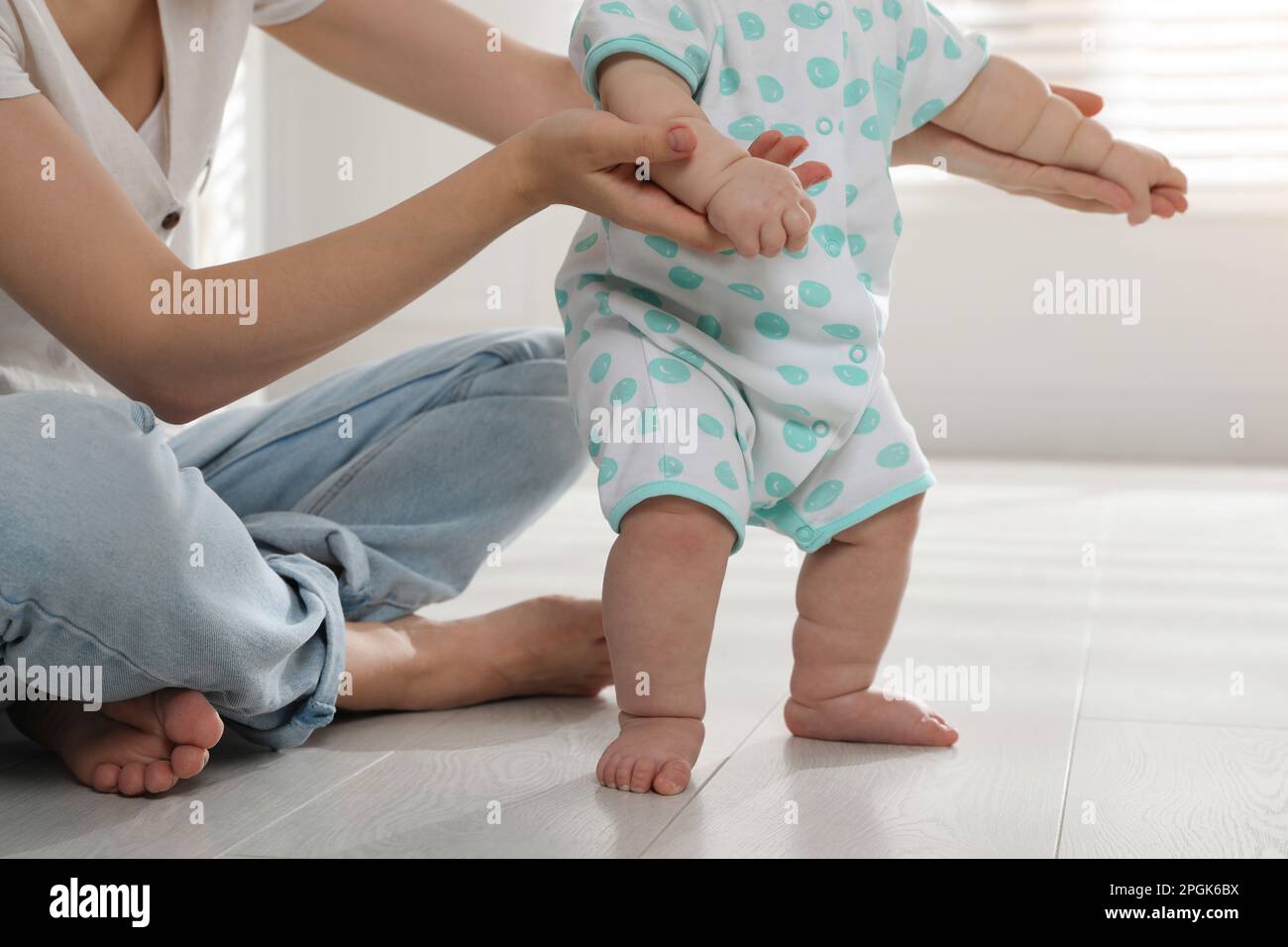 Mother supporting her baby daughter while she learning to walk at home ...