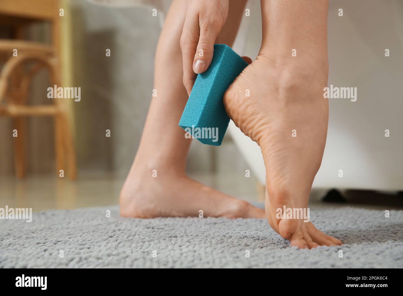 Woman using pumice stone for removing dead skin from feet indoors ...