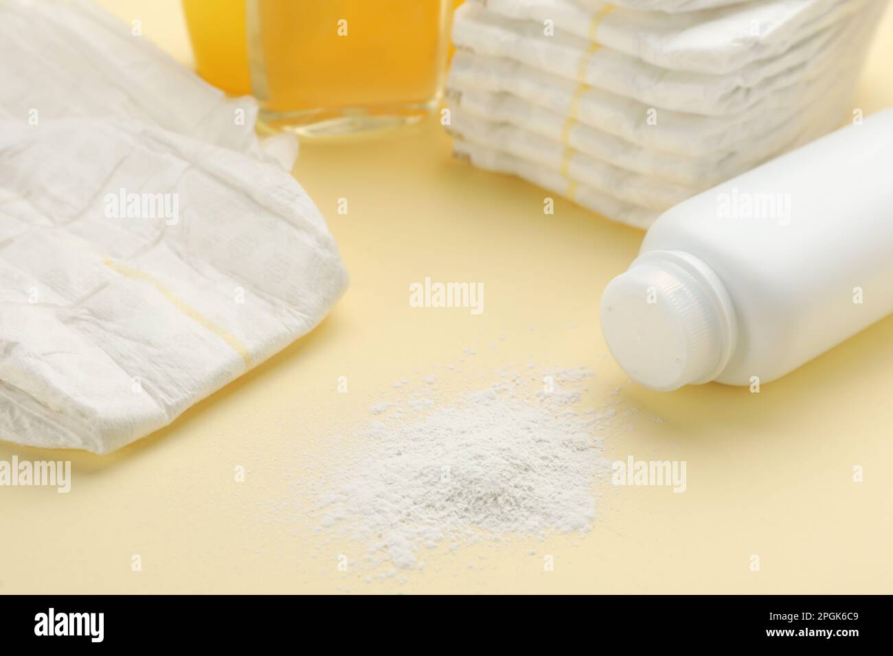 Bottle, scattered dusting powder and diapers on beige background. Baby ...