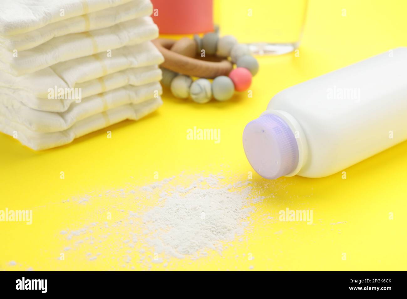 Bottle, scattered dusting powder and diapers on yellow background. Baby ...