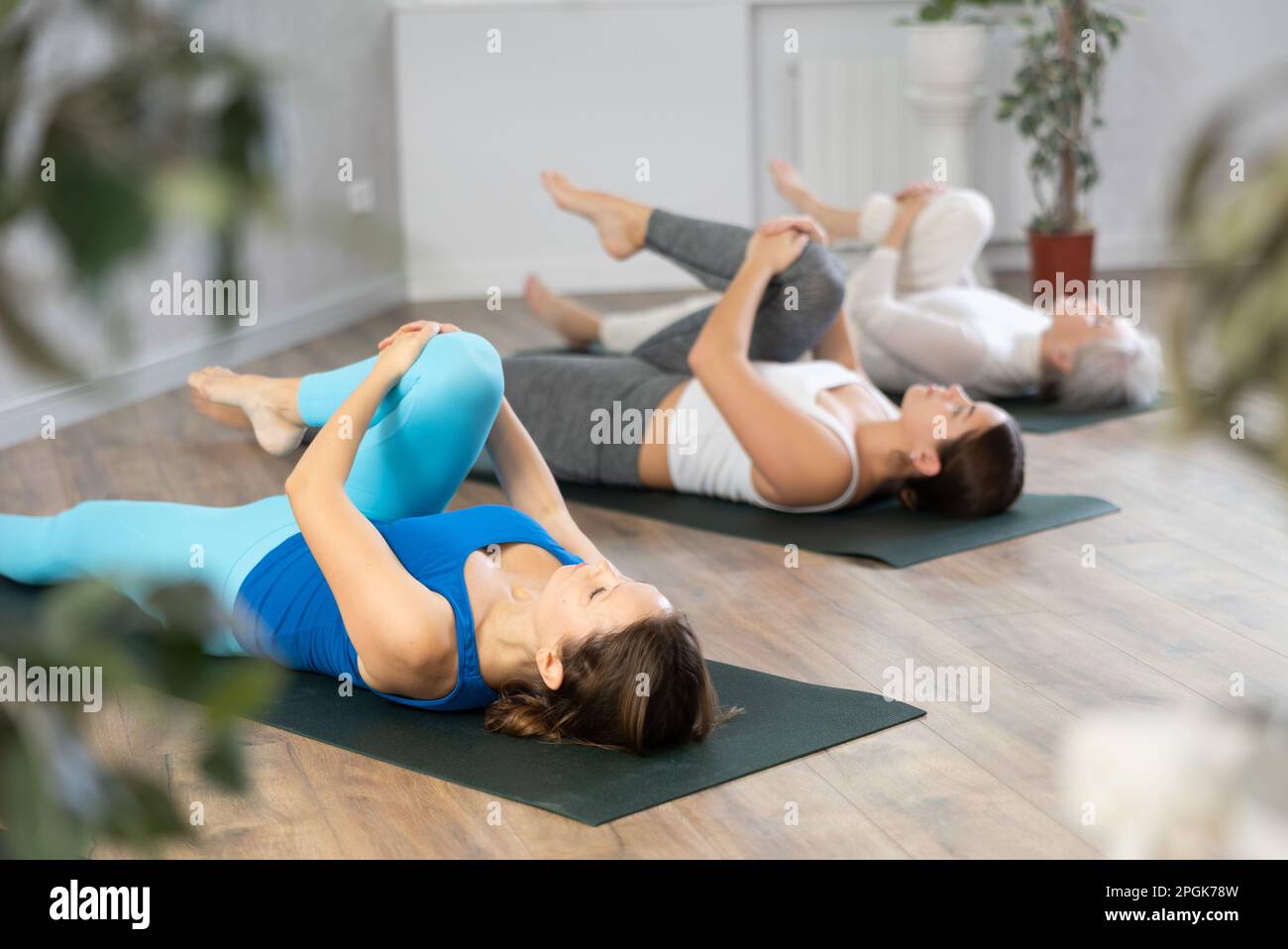 Diligent women practicing wind relieving pose of yoga in light fitness ...