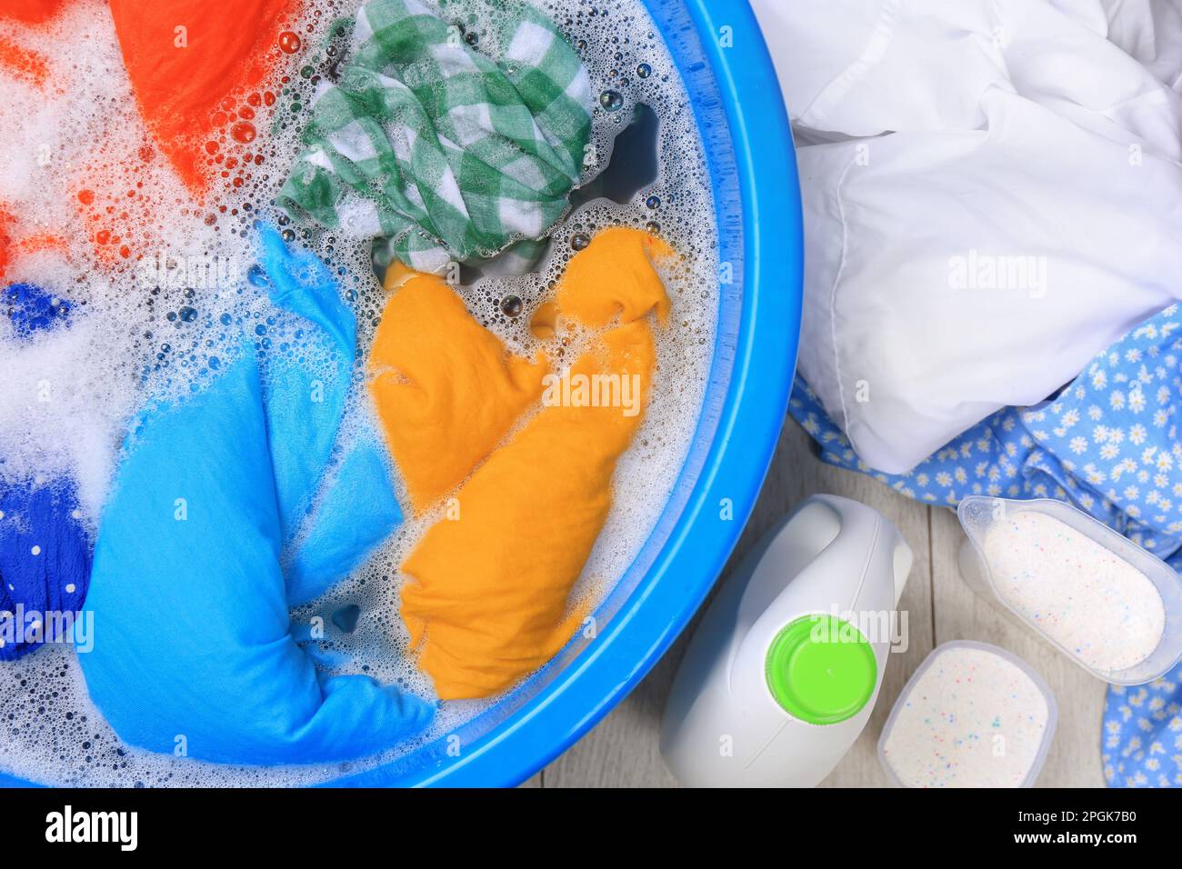 Basin with colorful clothes near bottle of detergent and powder on ...