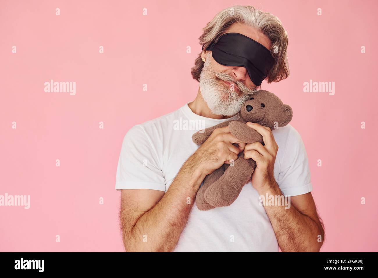 Holds teddy bear. Stylish modern senior man with gray hair and beard is ...