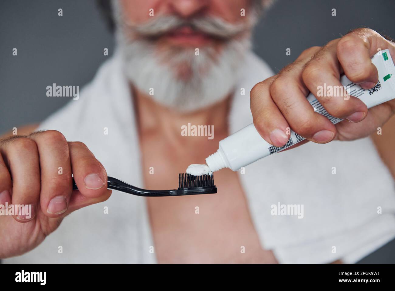 Using toothpaste. Stylish modern senior man with gray hair and beard is ...